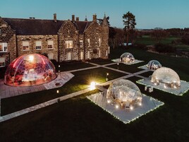 Um edifício histórico de pedra com um pátio que apresenta estruturas de cúpulas transparentes com assentos.