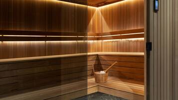 Uma sauna com bancos de madeira, um balde com escova e um painel digital na parede.