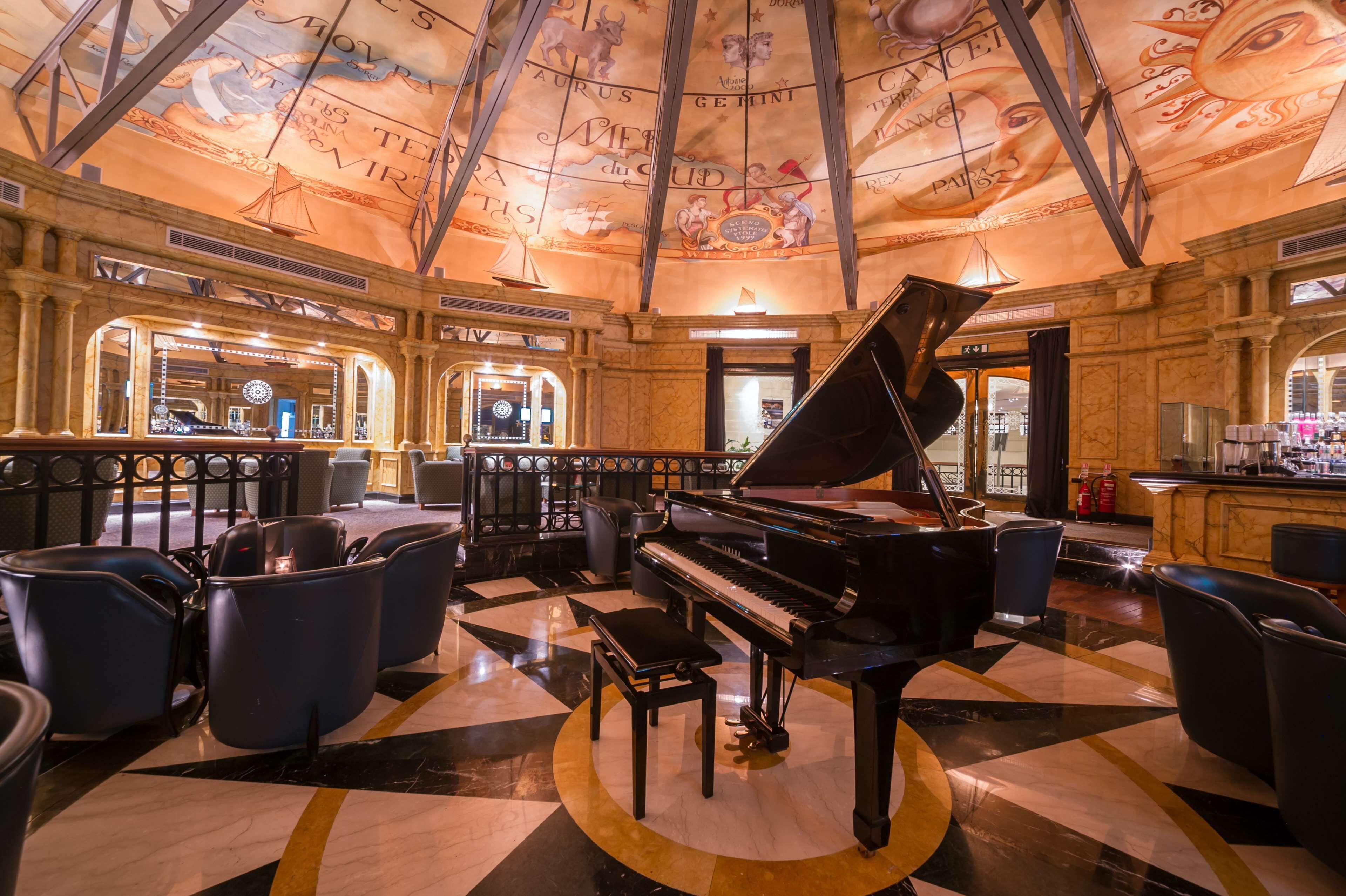 Um piano de cauda em um hall amplo com teto decorativo e área de estar.