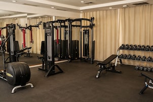 Uma academia com equipamentos de musculação, um banco e uma estrutura com halteres.