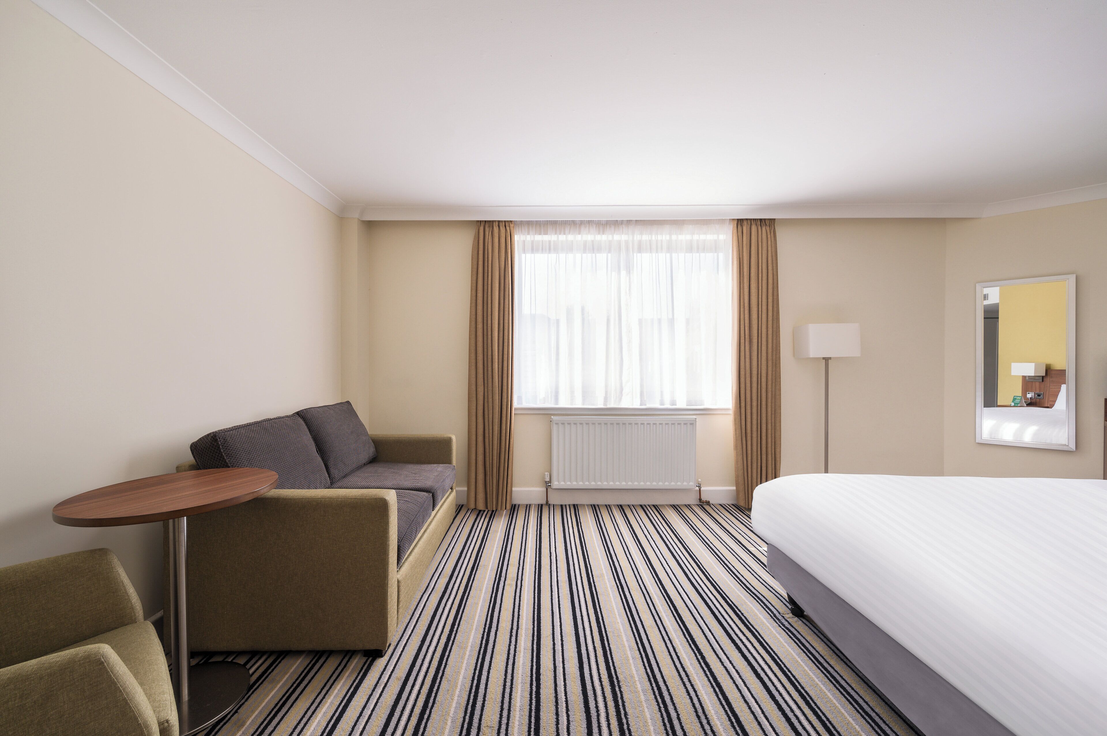 Quarto de hotel com cama, sofá, mesa pequena e radiador.