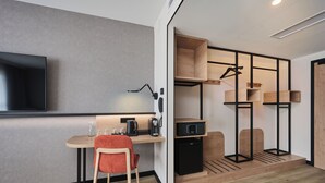 Quarto compacto com escrivaninha, cadeira, TV e prateleiras embutidas.