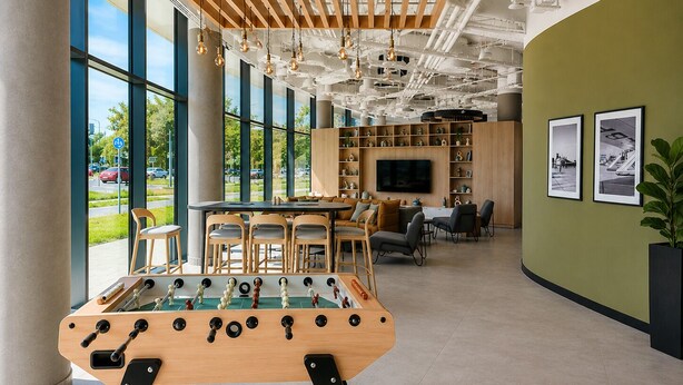 Um espaço moderno e interno com mesa de pebolim, área de estar e uma grande janela com vista para o exterior.
