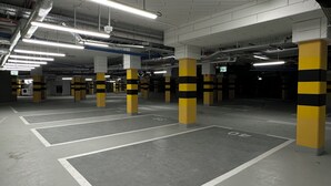 Garagem de estacionamento coberta com várias vagas, pilares listrados em amarelo e preto, e iluminação fluorescente.