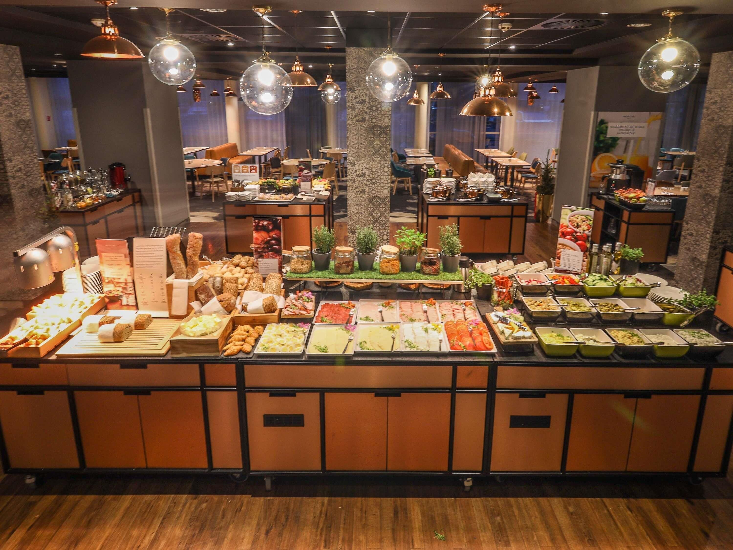 Uma área de buffet com diversas opções de comida, mesas e luminárias pendentes.