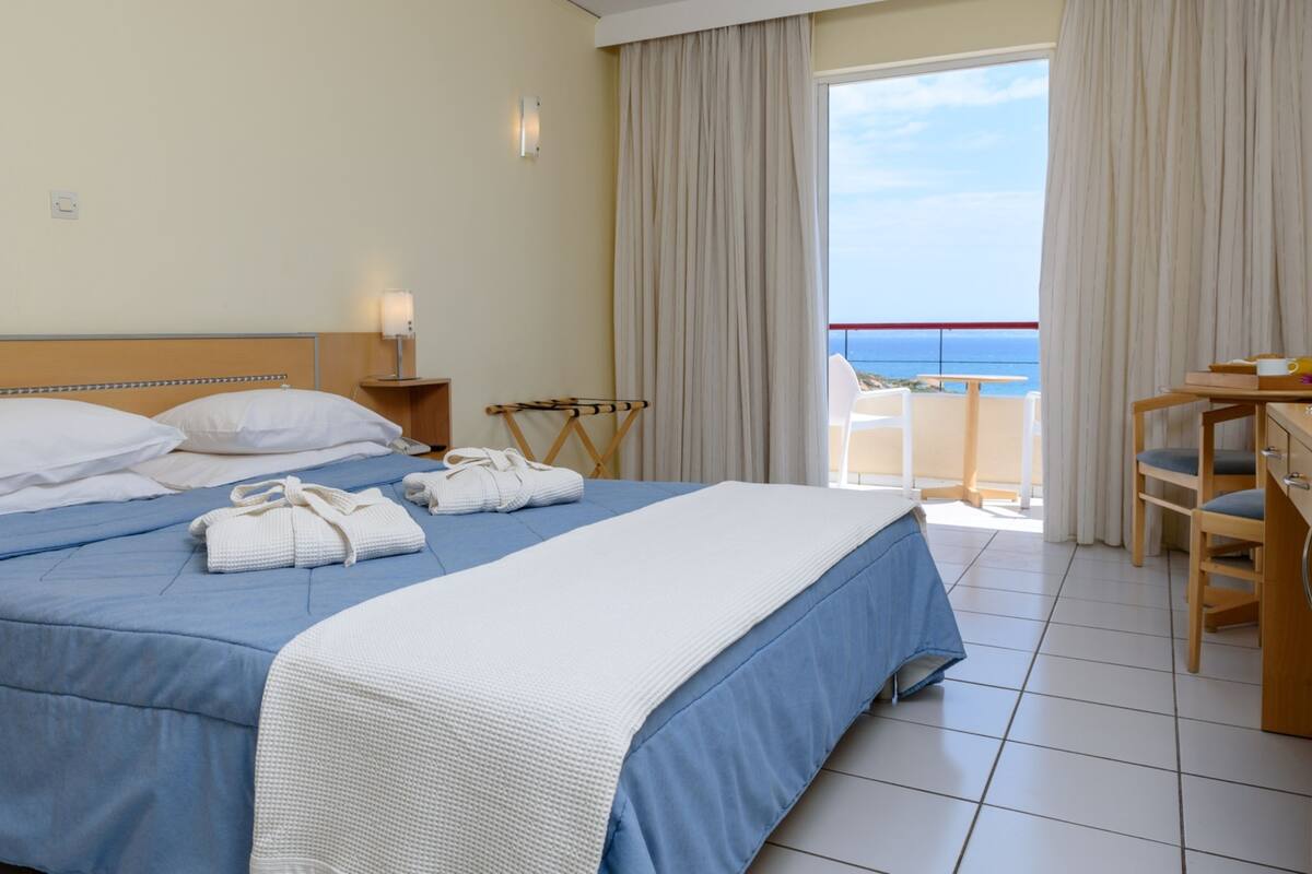 Quarto de hotel com cama, escrivaninha e vista para o mar.