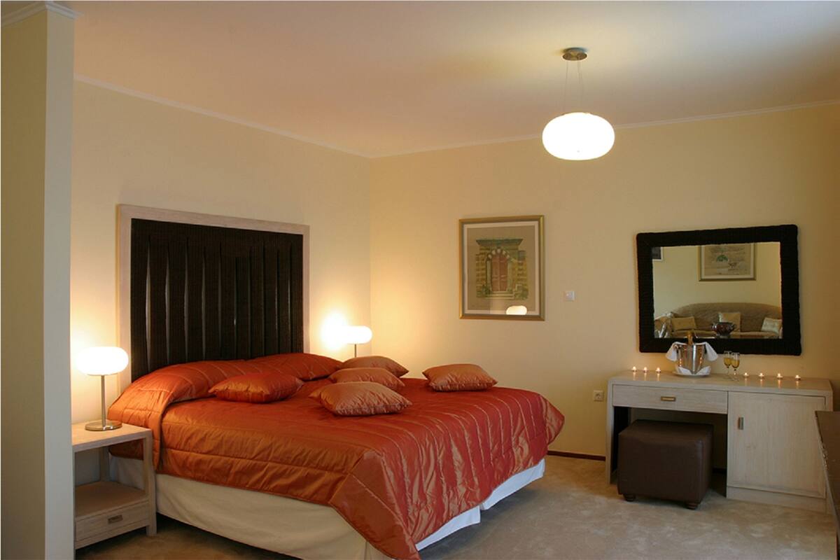Quarto com cama, abajures, cômoda, espelho e um quadro na parede.
