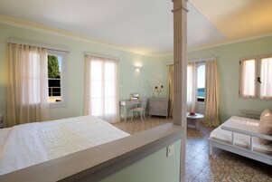 Quarto de hotel com duas camas, uma escrivaninha, uma cadeira, uma mesinha com um vaso de flores e vista para o mar.
