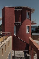 Um edifício vermelho com varanda, escadaria e vista para o mar.