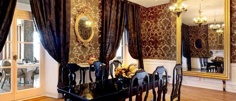 Uma sala de jantar com mesa preta, cadeiras ornamentadas e um espelho grande.
