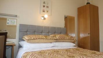Um quarto com cama, mesa de cabeceira, luminária na parede, quadro emoldurado e guarda-roupa de madeira.