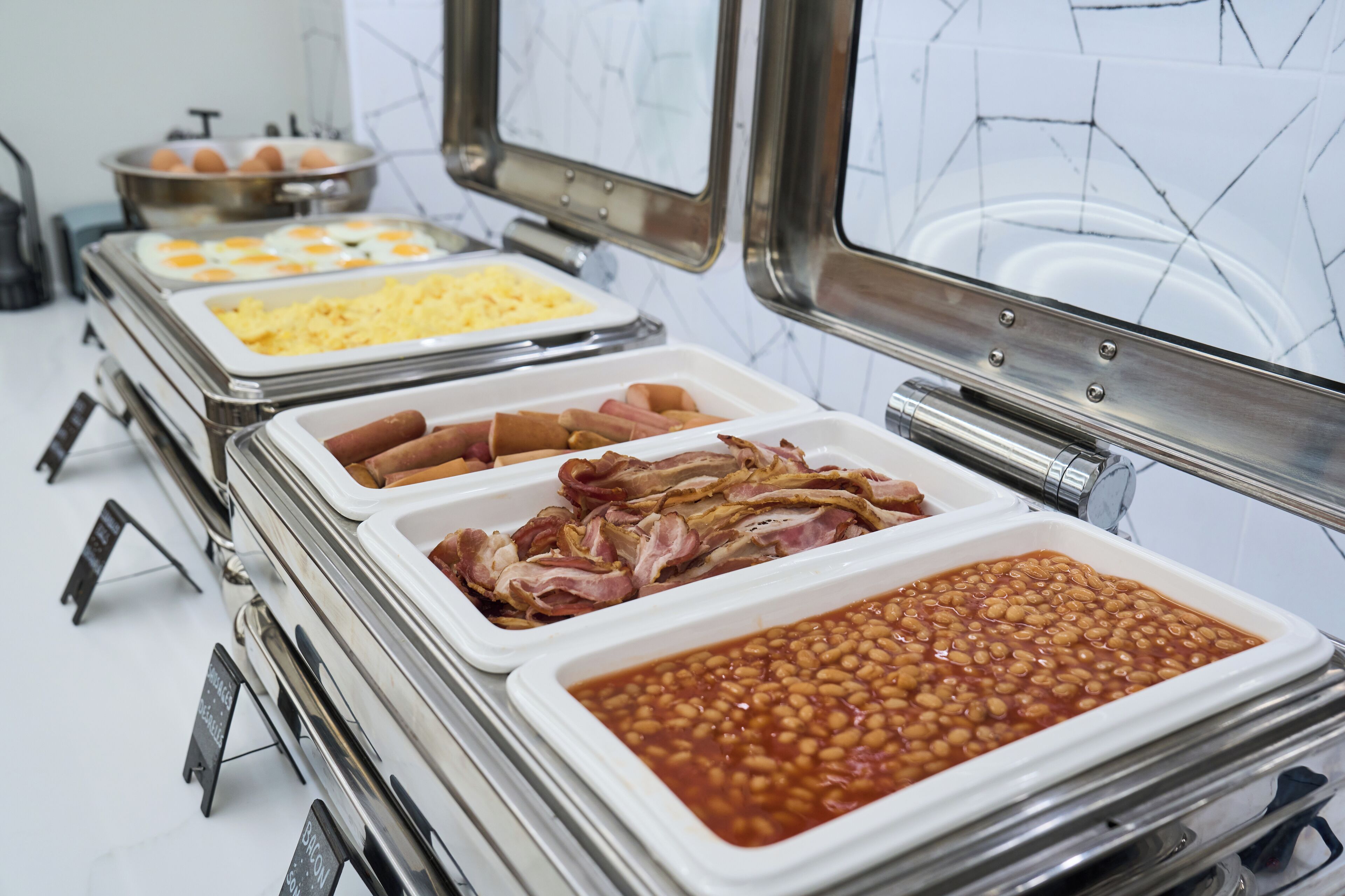 Buffet com diversas opções de comida, incluindo ovos, bacon e feijão.