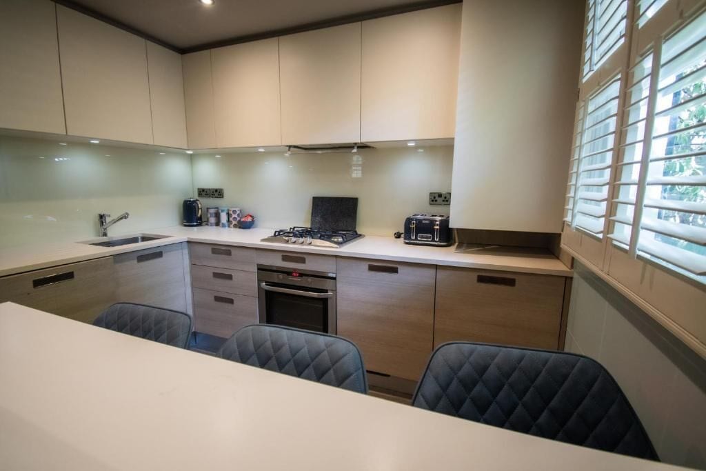 Cozinha moderna com ilha central, eletrodomésticos embutidos e espaço de jantar com duas cadeiras.