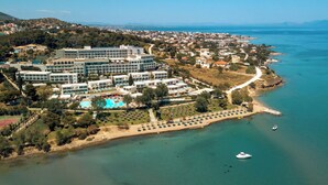 Vista aérea de um hotel à beira-mar, com vários edifícios, piscina e área de praia com guarda-sóis.