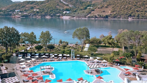 Área de piscina com espreguiçadeiras e guarda-sóis, cercada por vegetação e vista para um lago.