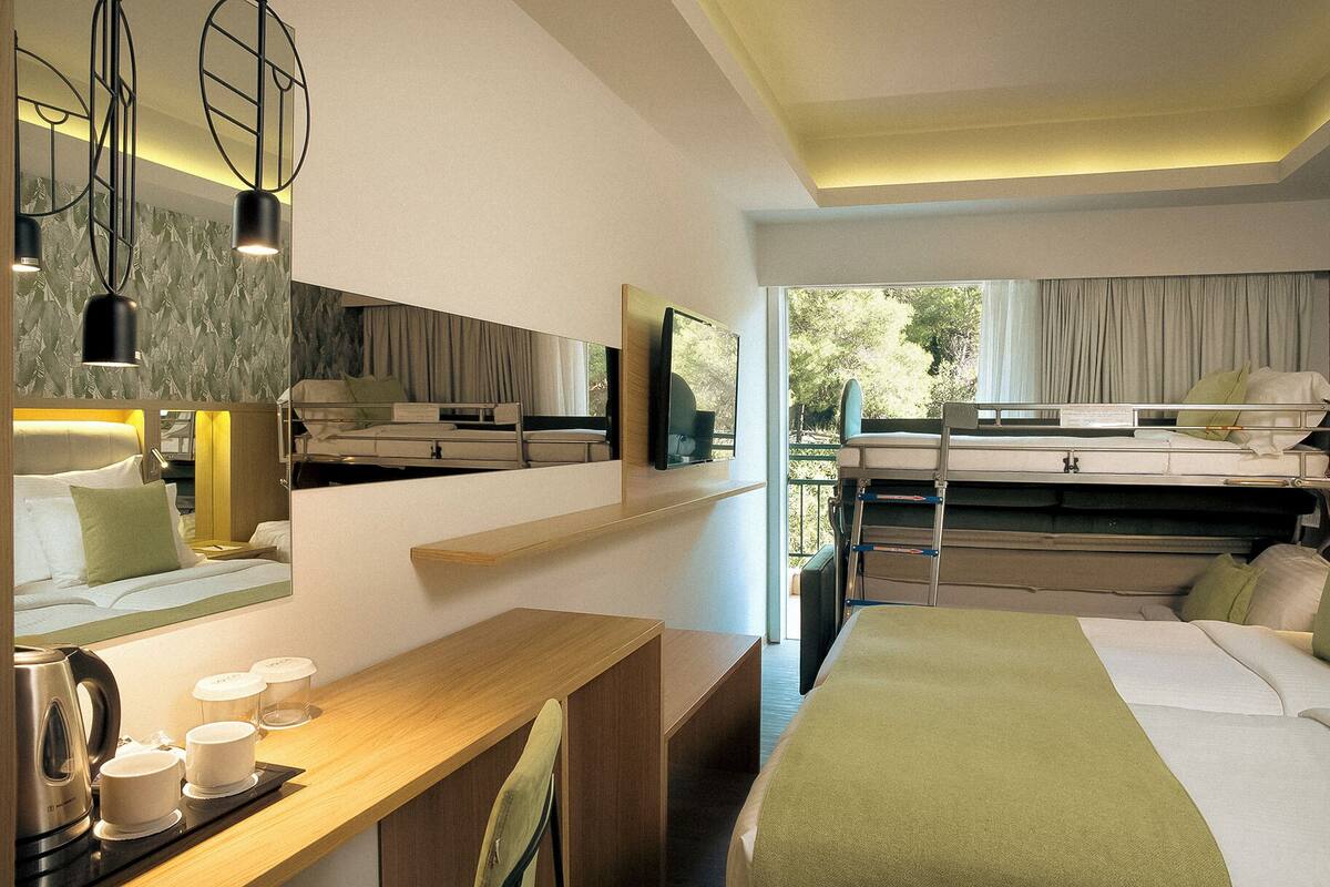 Quarto de hotel moderno com beliche, escrivaninha com chaleira e uma grande janela com vista para o exterior.