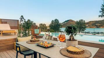 Uma área de refeições com uma mesa posta para dois, piscina e vista para o mar e colinas.