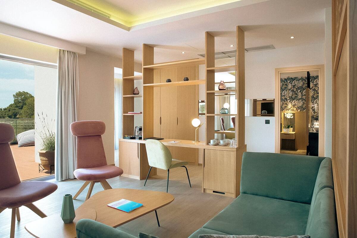 Uma sala de estar moderna com sofá, poltronas, mesa de centro e um espaço de trabalho com estantes e abajur.