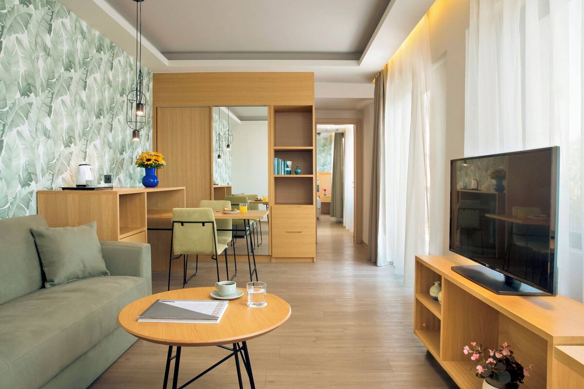 Uma sala de estar moderna com um sofá, uma área de jantar com cadeiras, uma televisão em um móvel e uma estante de livros.