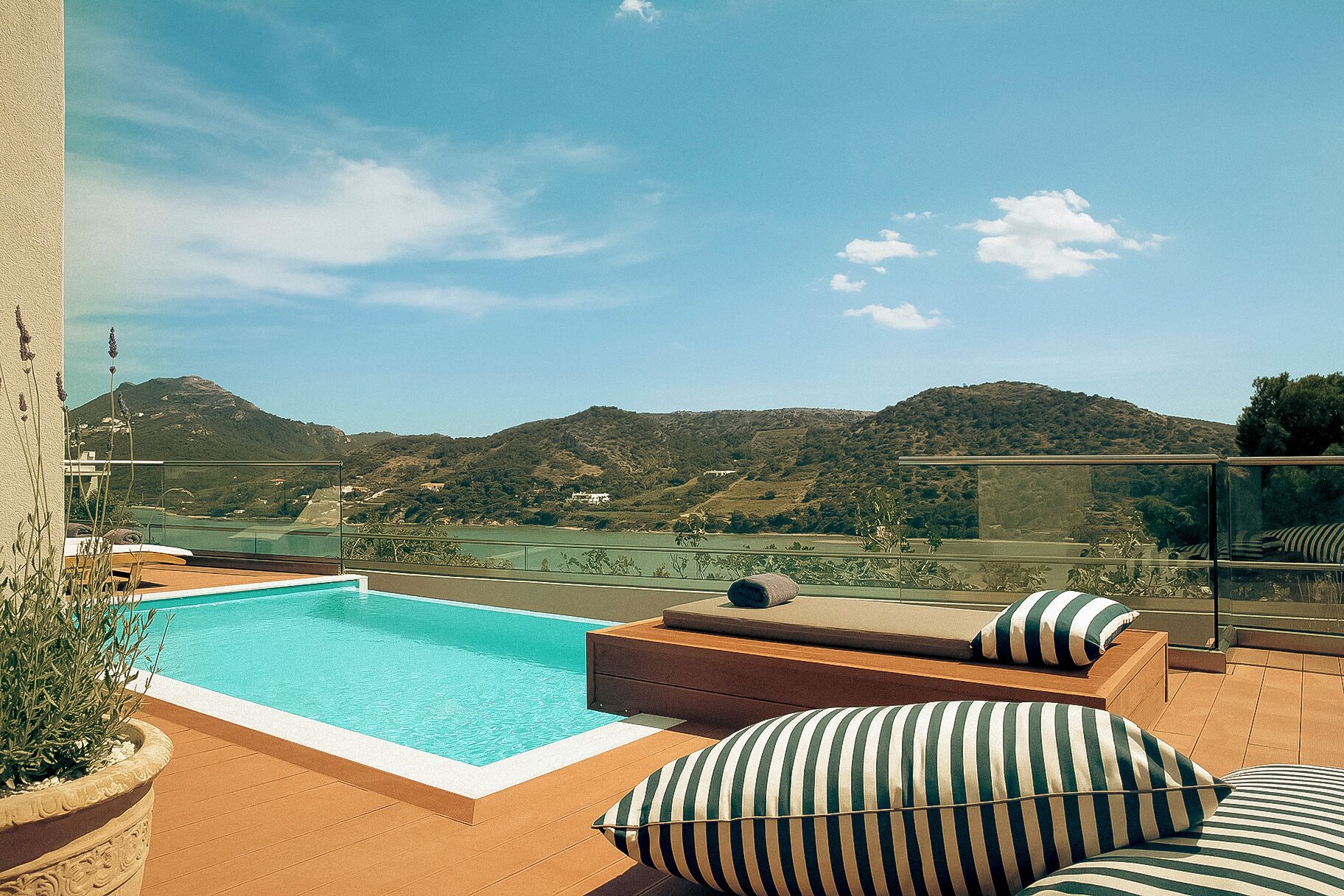 Piscina no terraço com vista para montanhas, guarda-corpo de vidro e almofadas listradas.