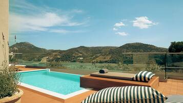 Piscina no terraço com vista para montanhas, guarda-corpo de vidro e almofadas listradas.