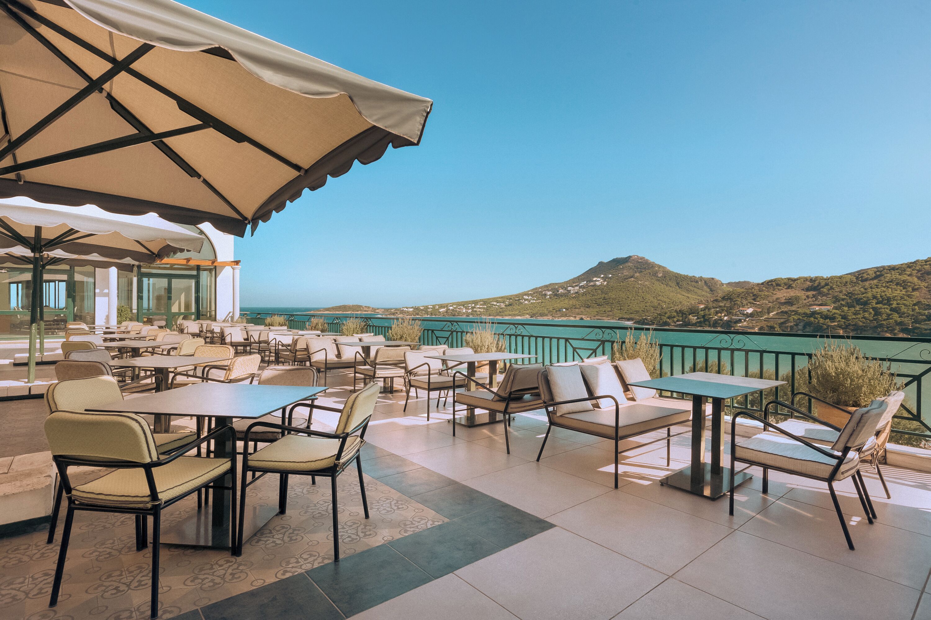Terraço ao ar livre com mesas e cadeiras, com vista para uma paisagem pitoresca com colinas e um corpo de água.