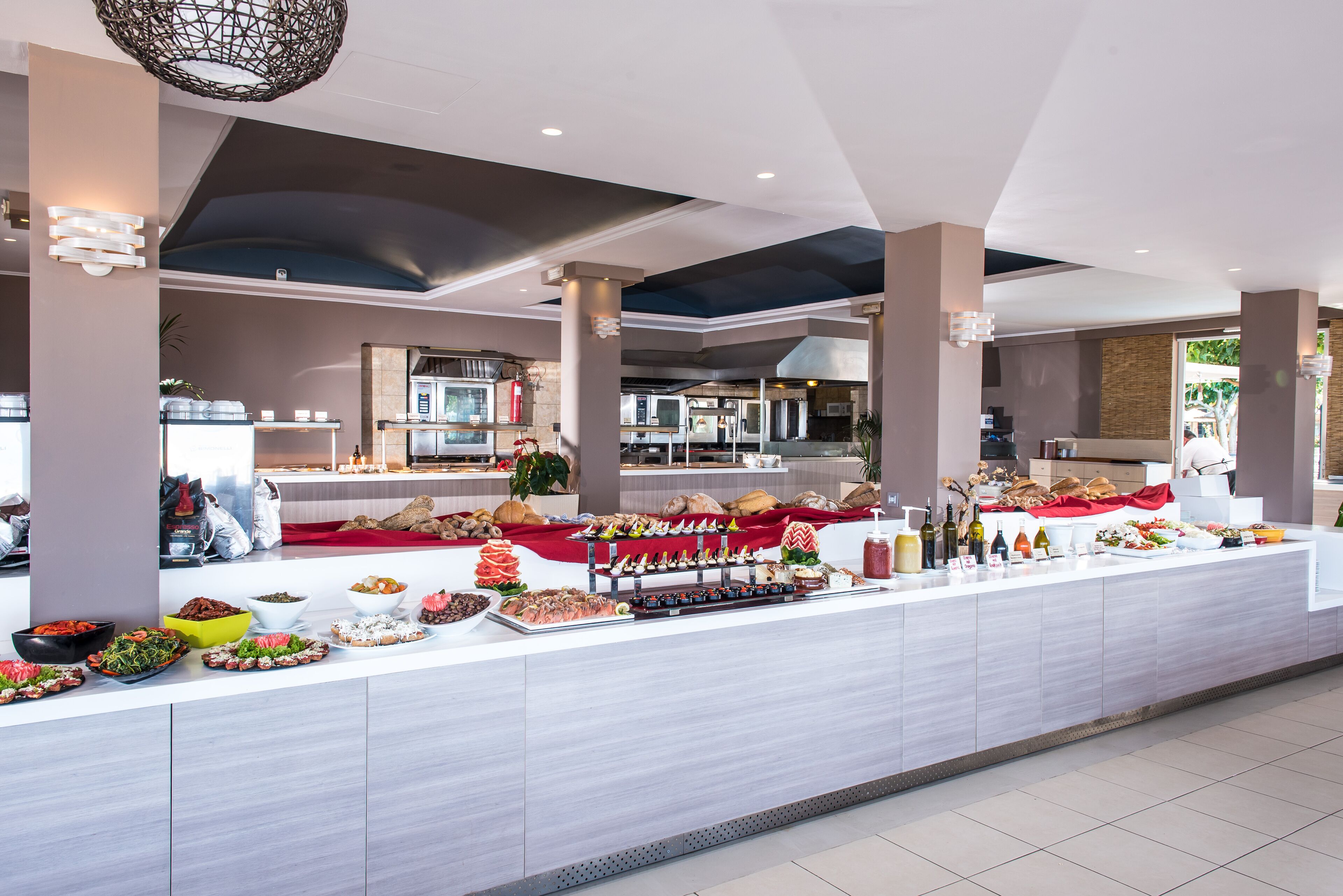 Disposição de buffet com diversos alimentos e área de cozinha ao fundo.