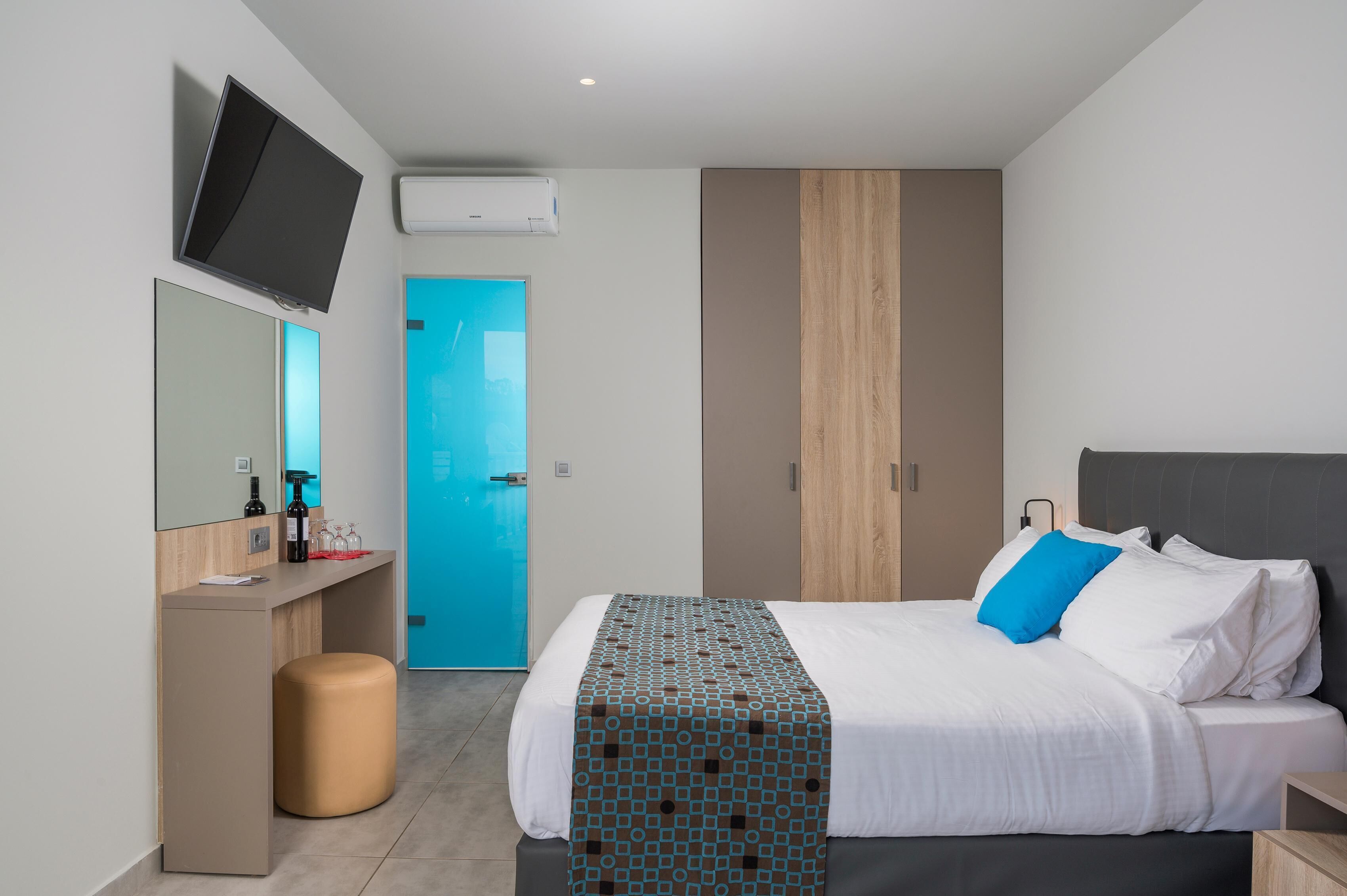 Quarto de hotel moderno com cama, televisão na parede, secretária com espelho e armário.
