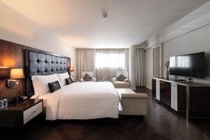 Quarto de hotel moderno com uma cama grande, TV, escrivaninha e área de estar.
