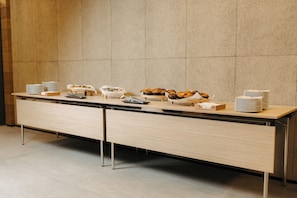 Uma mesa de buffet com pratos, tigelas e uma bandeja de muffins em frente a uma parede azulejada.