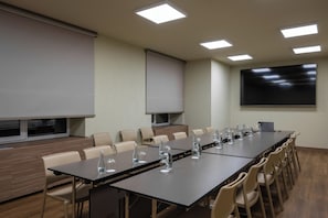 Uma sala de conferências com uma mesa comprida, cadeiras, um projetor e uma televisão.