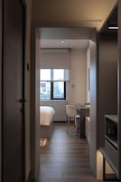 Quarto de hotel moderno com piso de madeira, uma cama, uma escrivaninha e uma janela com persianas.