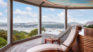 Quarto moderno com uma grande janela com vista para a cidade, um espaço de estar acolchoado e uma pequena mesa com um vaso.