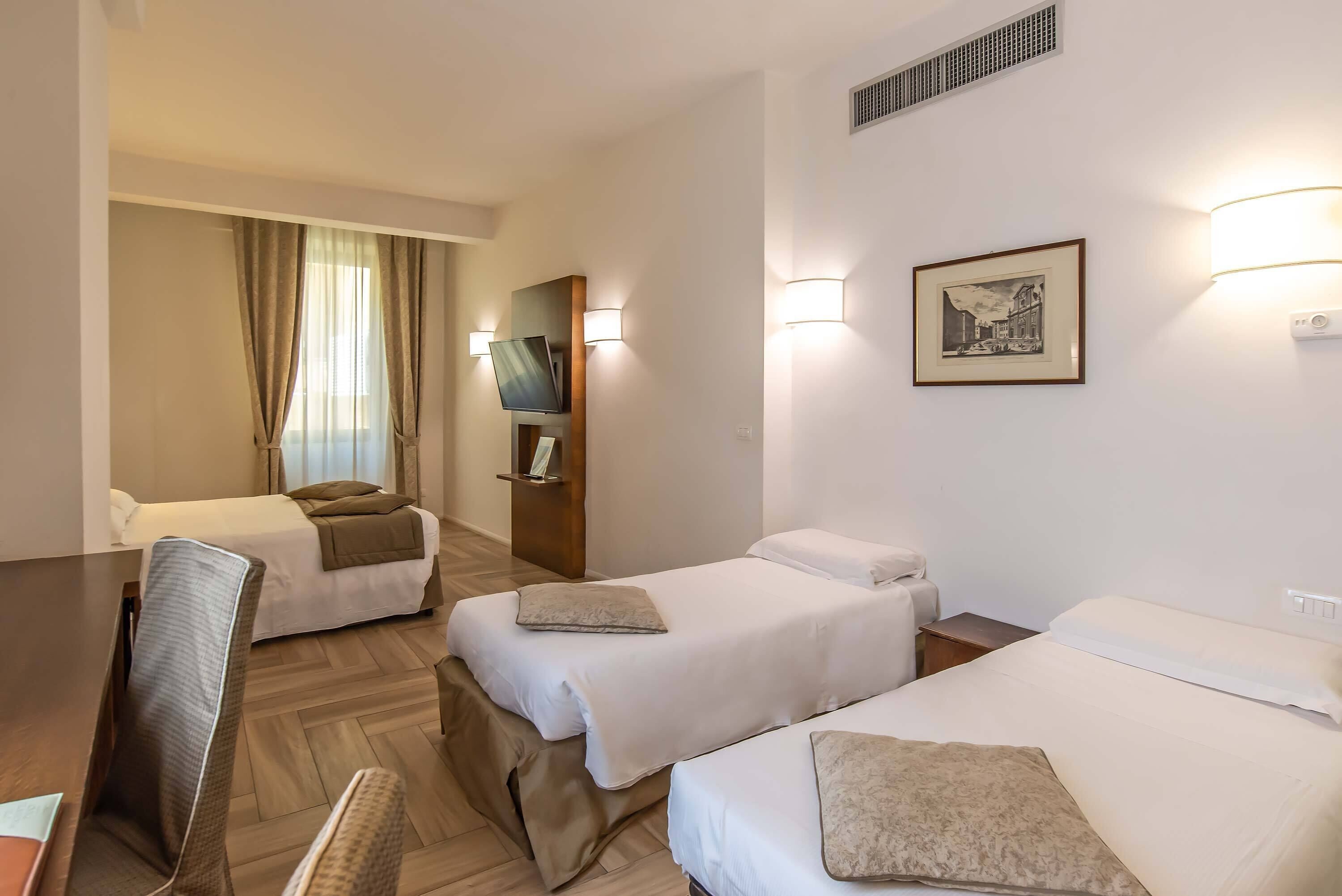Quarto de hotel com duas camas de solteiro, uma escrivaninha, uma cadeira, televisão e um quadro na parede.