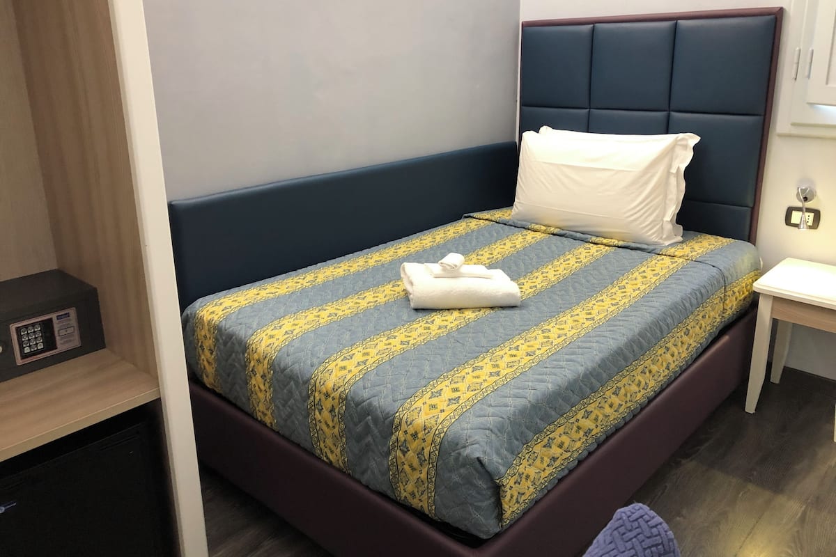Uma cama bem arrumada com um cobre-leito estampado, um travesseiro branco e uma toalha dobrada sobre a cama.