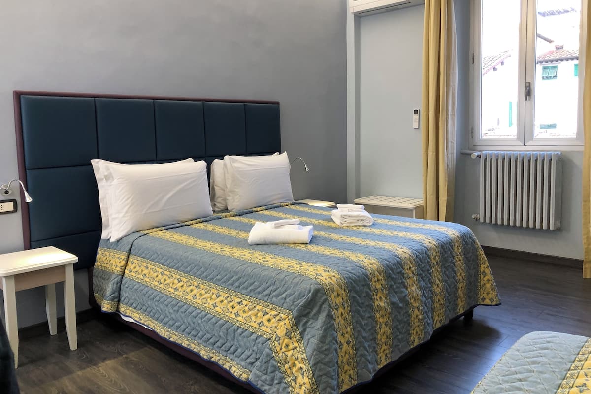 Uma cama bem arrumada com colcha azul e amarela estampada, travesseiros brancos e uma toalha dobrada em uma mesa de cabeceira.