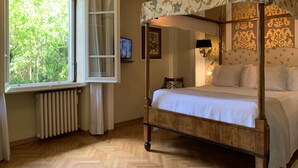 Uma cama de dossel com teto, um radiador, uma televisão sobre uma prateleira e uma janela com cortinas.