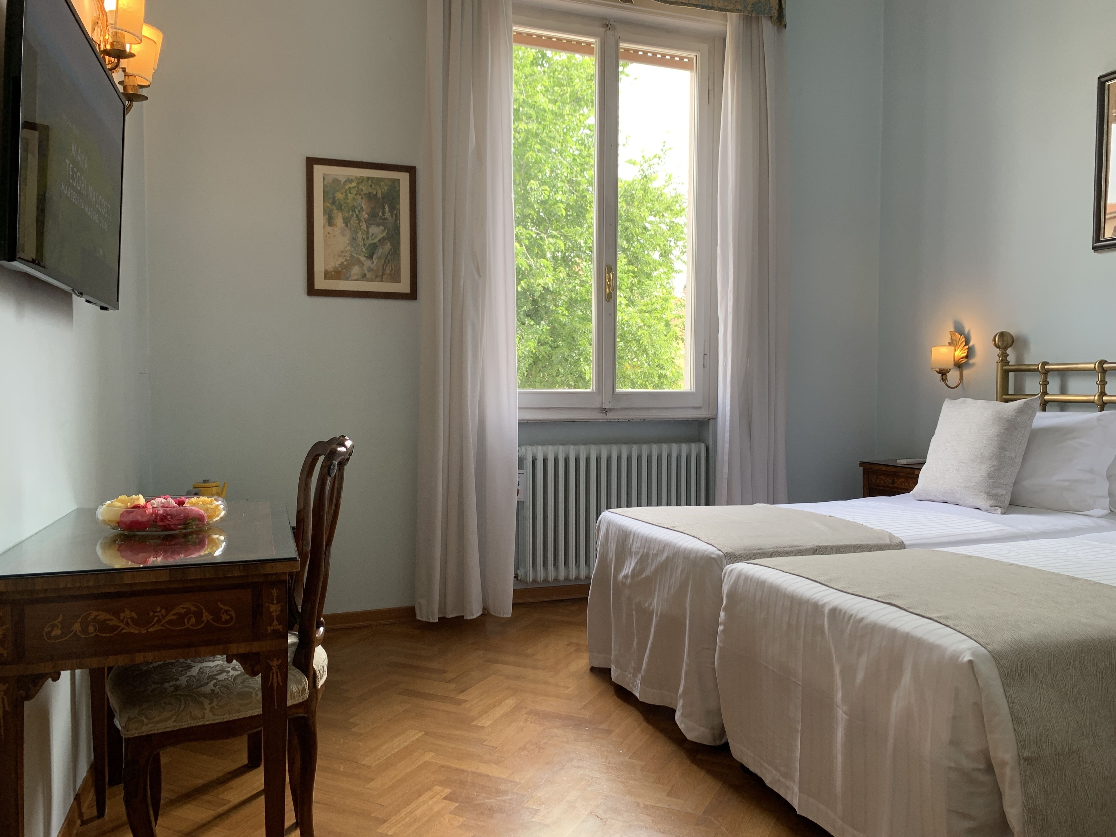 Quarto com duas camas, uma escrivaninha de madeira com cadeira, um radiador e uma janela com cortinas.