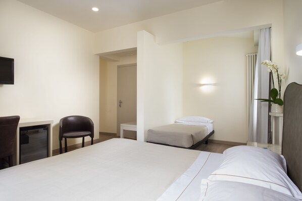 Quarto de hotel com cama, escrivaninha, cadeira e televisão.