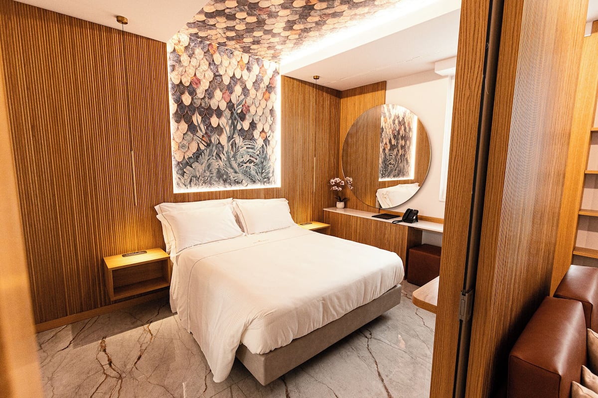 Quarto moderno com uma cama grande, painéis de madeira, um espelho redondo e parede com padrão de pedra.