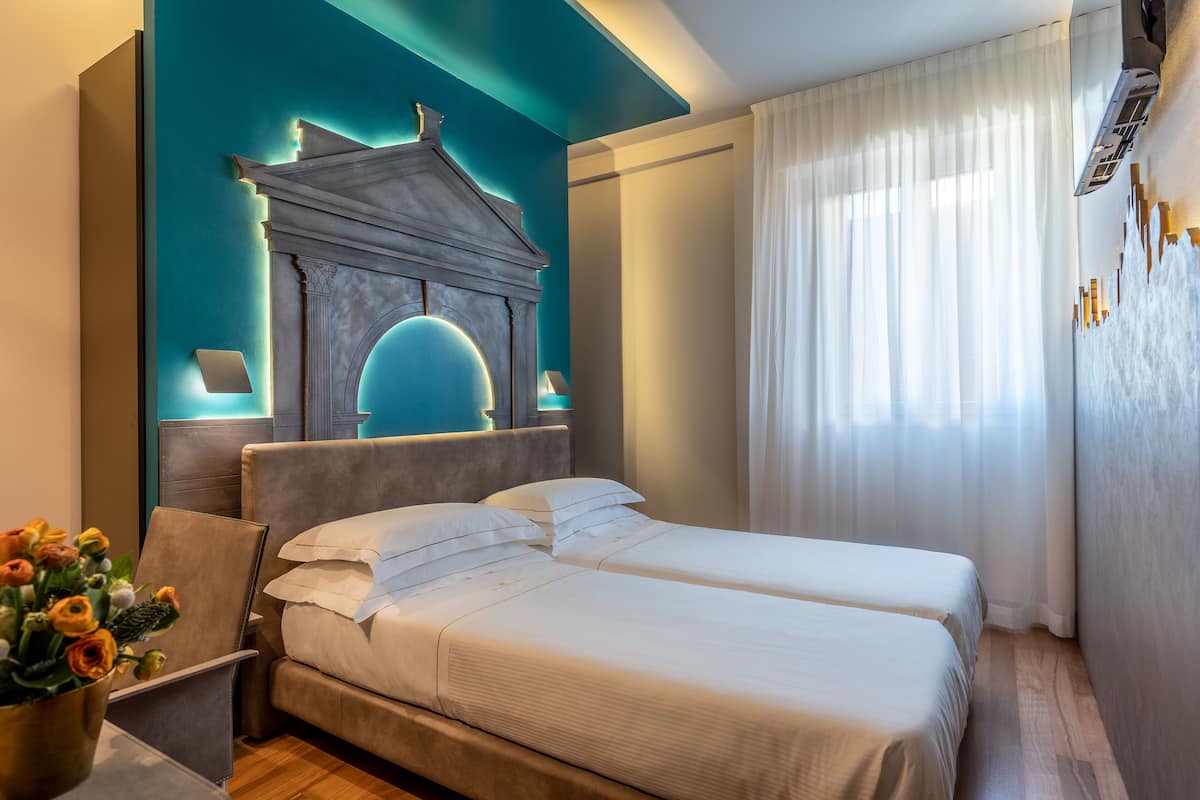 Quarto de hotel com uma cama grande, uma mesinha de cabeceira, um vaso de flores e uma lareira decorativa.