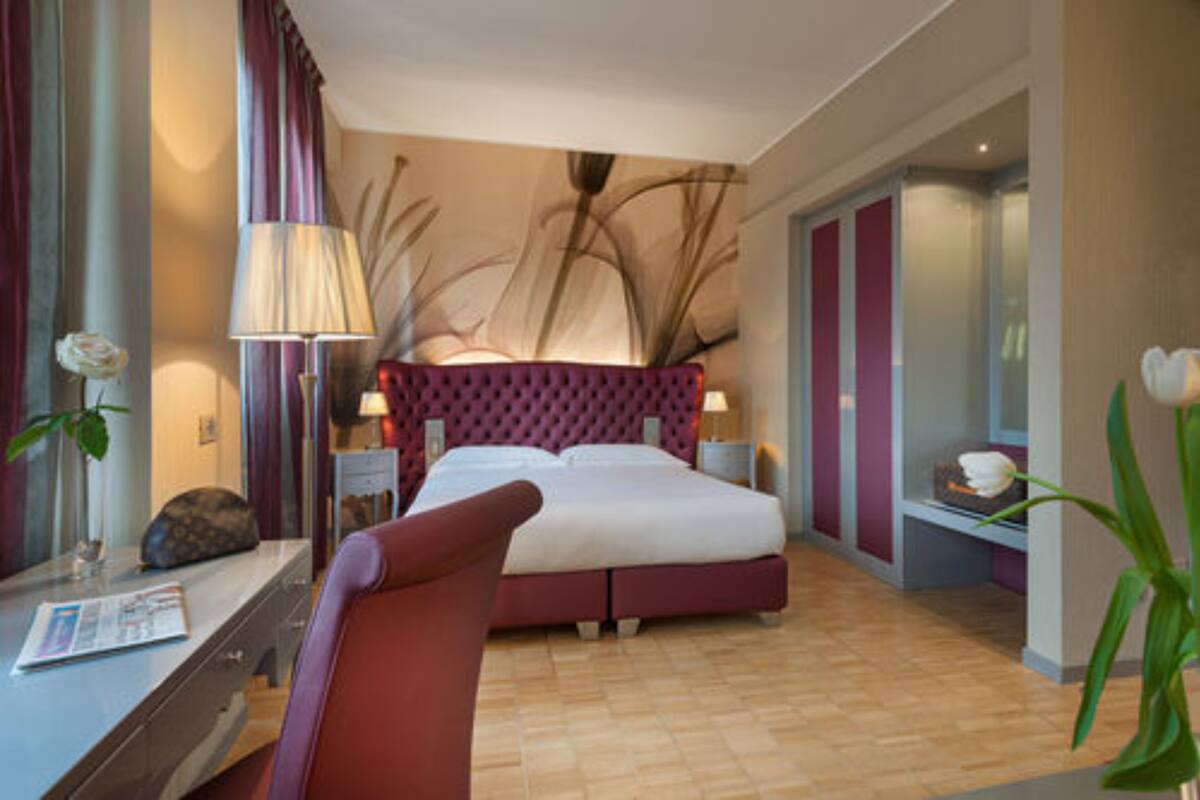 Quarto de hotel com uma cama grande, uma escrivaninha, uma cadeira, um abajur e um espelho.