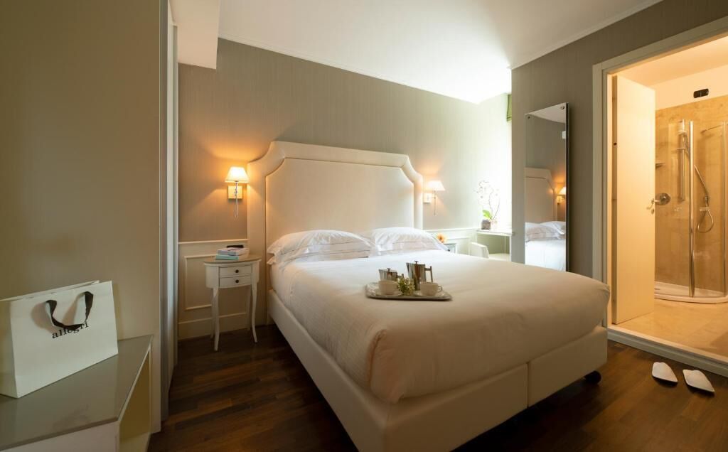 Quarto de hotel com cama, mesa de cabeceira, luminária e área de chuveiro.