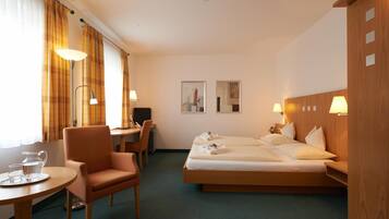 Quarto de hotel com cama, escrivaninha, cadeira e mesa com um copo e jarra.