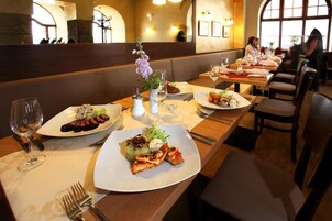 Interior de restaurante com mesas postas para refeições, com pratos de comida e copos de vinho.
