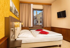 Quarto de hotel com cama, televisão e janela com cortinas.