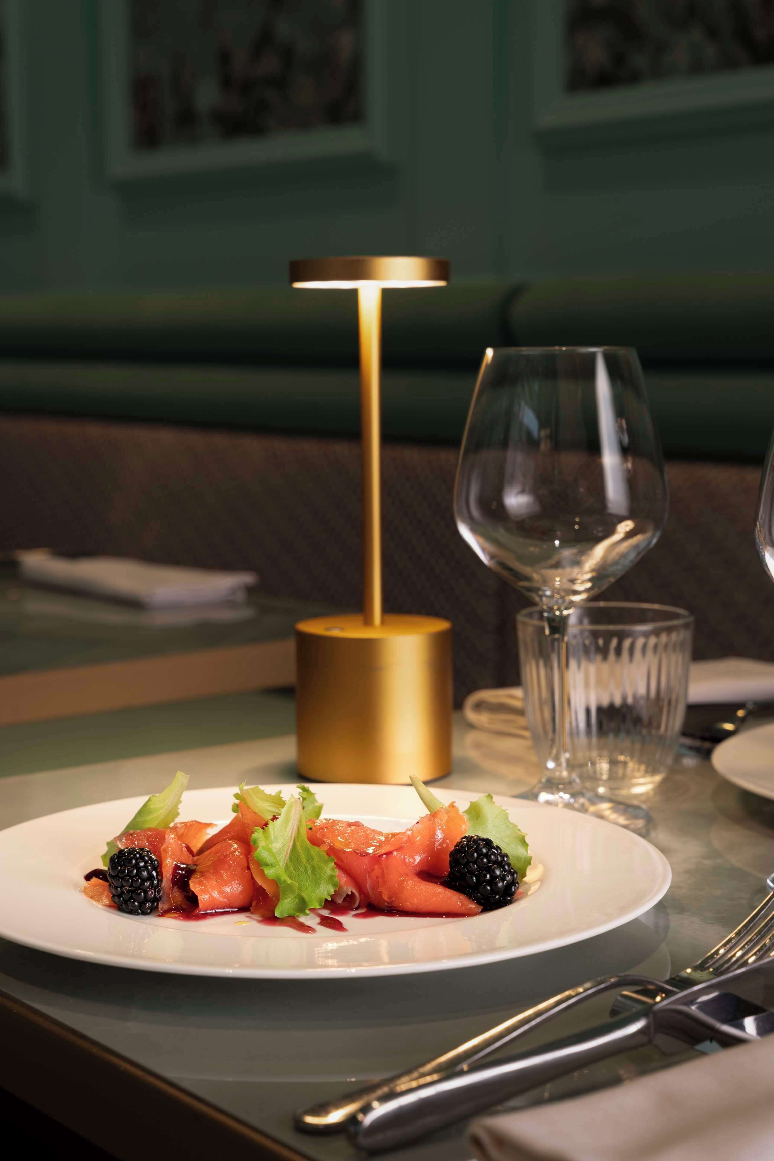 Uma mesa de jantar com um prato de comida, um copo de água e um abajur dourado.