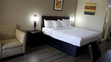Quarto de hotel com cama, uma cadeira, mesa de cabeceira e duas luminárias fixadas na parede.