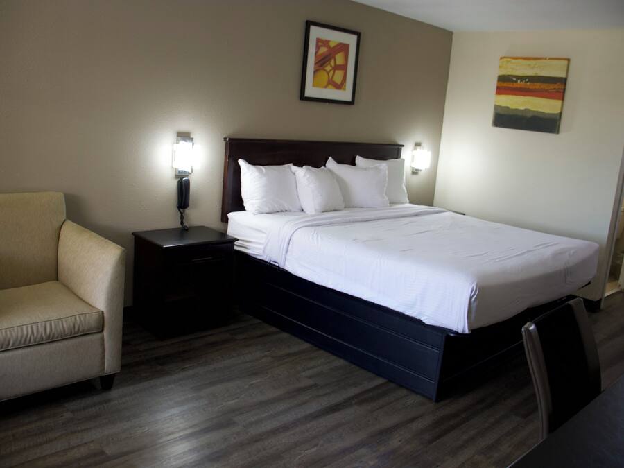 Quarto de hotel com cama, uma cadeira, mesa de cabeceira e duas luminárias fixadas na parede.