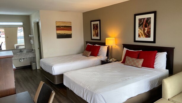 Quarto de hotel com duas camas, uma escrivaninha e uma cadeira. Há quadros nas paredes e uma luminária sobre a escrivaninha.